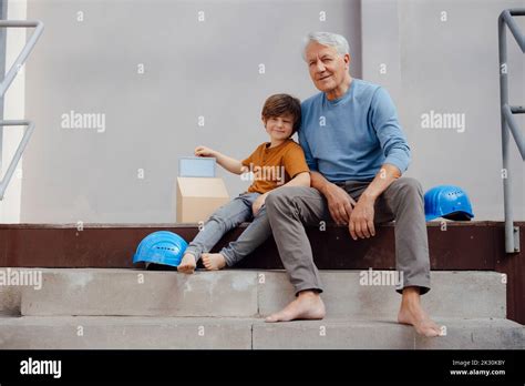 Grandfather And Grandson With Solar Model House Sitting On Staircase
