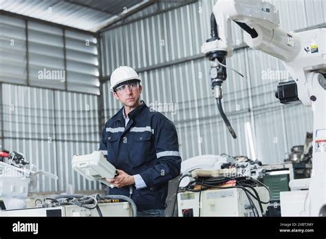 Engineer Controlling Robot Arm At Factory Checking The Operation Of