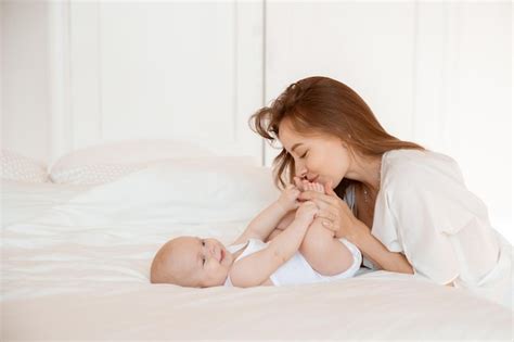 Mamá besa las piernas del bebé en casa en el dormitorio Foto Premium