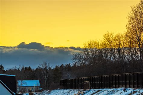 눈 덮인 풍경 위로 황금빛 하늘이 있는 겨울 일몰 실루엣이 있는 나무와 시골 환경에서 조명이 켜진 집 스웨덴 0명에 대한 스톡