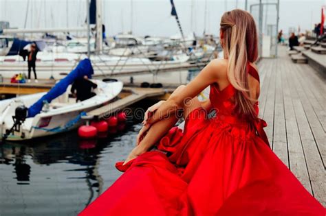 Young Gorgeous Woman In Long Red Dress Sitting On The Pier Stock Image