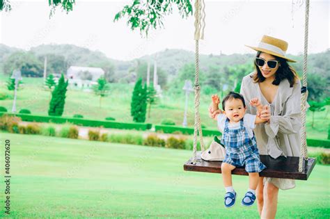 Happy Asian Mother And Son Smile Playing Swing Together In The Park In
