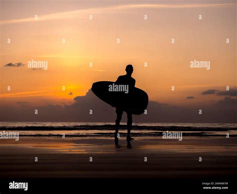 Man Silhouette Holding Surfing Board Walking On Dark Seashore Surfer