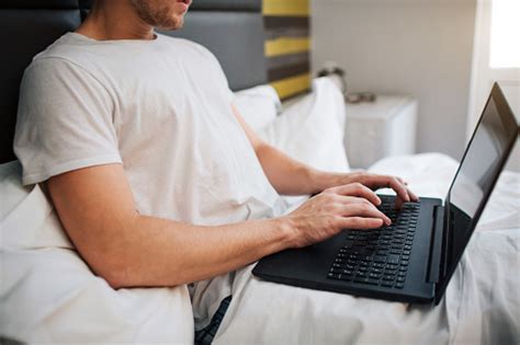 오늘 아침에 침대에서 젊은 남자의 절단 보기 그는 노트북을 들고 키보드에 입력 하 여 작동 합니다 재택 근무 일광 가리기에 대한