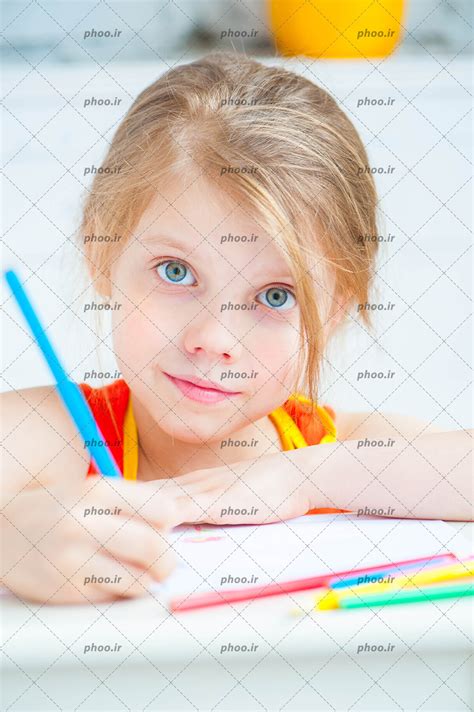 عکس با کیفیت چهره دختر بچه نشسته پشت میز در حال نقاشی کشیدن عکس با