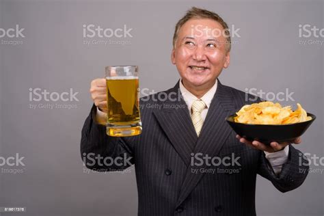 회색 배경 맥주의 유리 및 감자 칩의 그릇을 들고 성숙한 아시아 실업가의 스튜디오 샷 50 54세에 대한 스톡 사진 및 기타