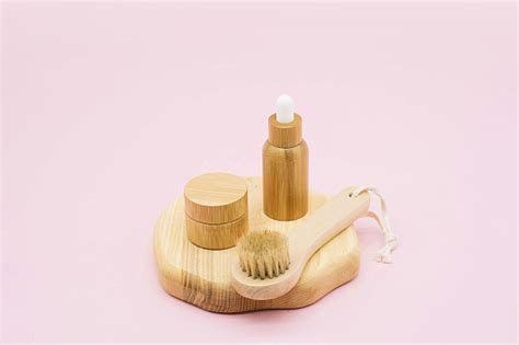 대나무 항아리 피펫이 있는 에센셜 오일 병 천연 드라이 페이스 브러쉬를 나무 연단에 파스텔 핑크 배경 유기농 스파 화장품 미용