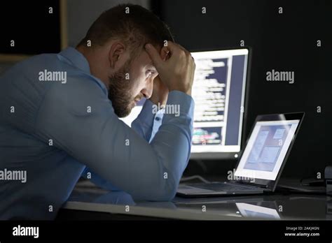 Worried Programmer Working Late At Night On Multiple Computer Screens
