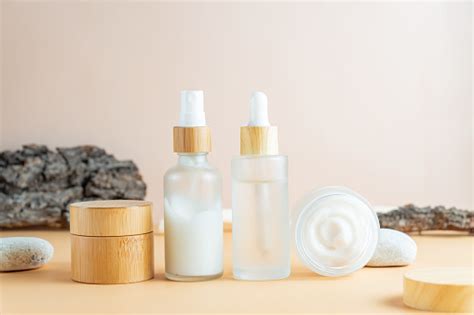 나무 껍질이있는 대나무 뚜껑이있는 흰색 서리가 내린 유리 화장품 병과 항아리 베이지 색 배경에 돌 노화된 피부를 위한 스킨케어