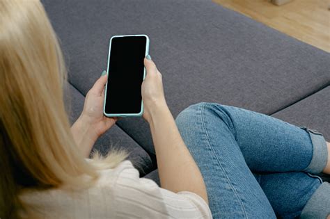 소파에 앉아있는 집에있는 여성은 스마트 폰을 사용하여 화상 통화를 통해 친척과 의사 소통을합니다 가족과 화상 통화를 하는 젊은 여성 Brand Name Smart Phone