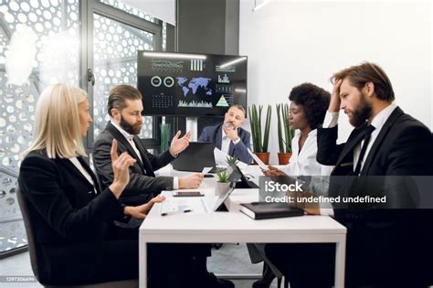 자신감 있는 남성과 여성 다민족 경제학자 또는 이사 사무실에서 브레인스토밍 중 회사 전략에 대해 논의하고 배경에 있는 월 Tv 화면에 세계지도 및 통계 차트 교육에 대한