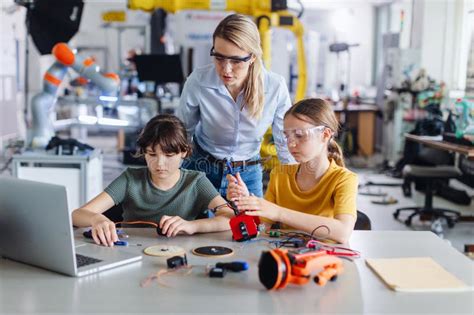 Female Teacher Helping To Girls Working On Small Robot Building