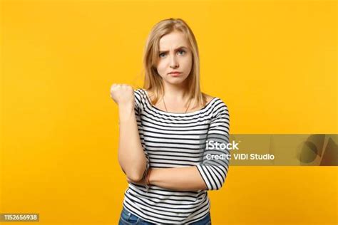 스튜디오에서 노란 주황색 벽 배경에 고립 된 주먹을 쥔 카메라를 찾고 줄무늬 옷에 관련 된 젊은 여자의 초상화 사람들은 진심으로