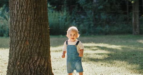일몰에 공원에 있는 거대한 큰 나무 아래에 서 있는 귀여운 아기 사랑스러운 미소를 짓는 한 살짜리 아이가 뒤뜰에서 야외를 걷고 있다 재미 있은 아이 정통 라이프 스타일