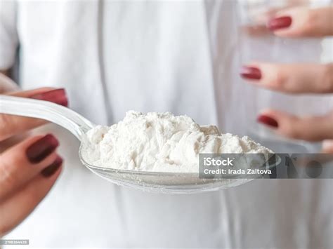 플라스틱 숟가락에 담긴 단백질 파우더를 손에 들고 배경에는 한 여성이 손에 물 한 컵을 들고 있습니다 단백질 식품 보충제 건강 보조 식품 건강한 생활방식에 대한 스톡 사진