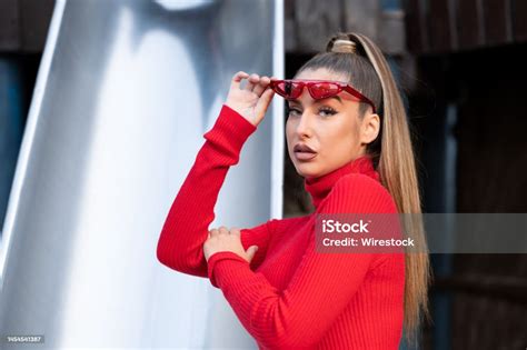 빨간 터틀넥과 선글라스를 쓴 매력적인 백인 여성이 놀이터 미끄럼틀 근처에서 포즈를 취하고 있다 관능에 대한 스톡 사진 및 기타 이미지 Istock