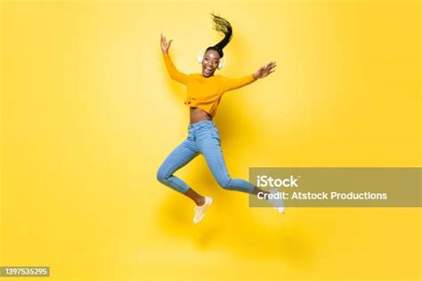 행복한 아프리카 계 미국인 여성의 전신 초상화 음악을 듣고 노란색 고립 된 스튜디오 색상 배경에서 손을 들고 뛰어 오르십시오 아프리카계 미국 민족에 대한 스톡 사진 및 기타