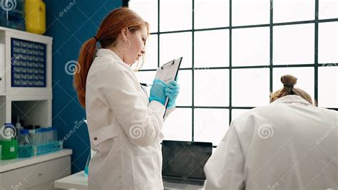 Man And Woman Wearing Sciencist Uniform Writing On Clipboard At