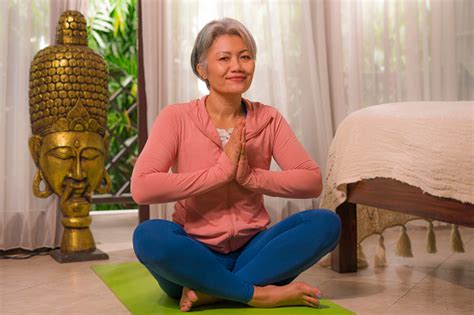 홈 라이프 스타일 아시아 데코 침실에서 요가와 명상 운동을하고 그녀의 50 년대에 회색 머리와 아름답고 행복한 성숙한 여성은 웰빙과 건강한 노화의 평화롭고 균형을 느끼고