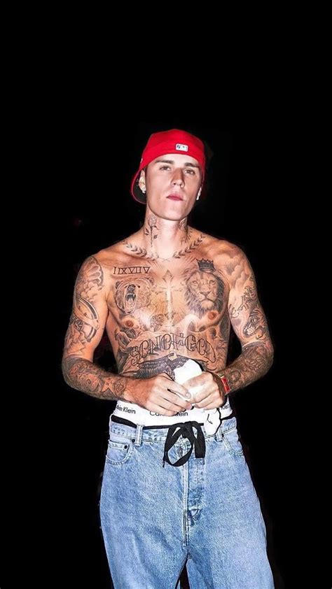 A Shirtless Man With Tattoos On His Chest Standing In Front Of A Black