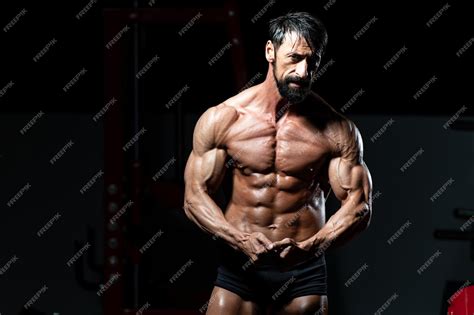 체육관에서 강하게 서 있고 근육을 구부리는 잘 생긴 성숙한 남자 근육 운동 보디 빌딩 피트니스 모델 운동 후 포즈 프리미엄 사진