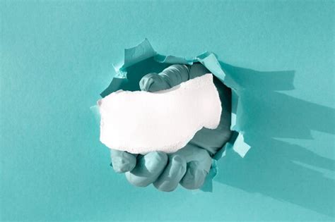Premium Photo Hand In Glove Through Paper Hole Holding Torn Piece Of