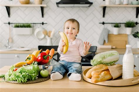 과일 및 야채와 그녀의 손에 바나나를 들고 사이 부엌에서 테이블에 앉아 1 년 된 여자 어린 소녀는 혀를 보여줍니다 가정 생활에 대한 스톡 사진 및 기타 이미지 Istock