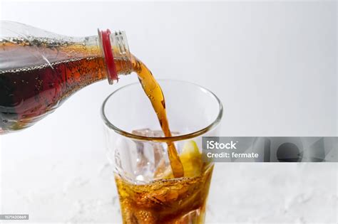 얼음 조각과 레몬 슬라이스가 있는 술잔에 병에서 신선한 콜라를 붓고 밝은 회색 배경에 상쾌한 음료를 마시고 복사 공간 선택한