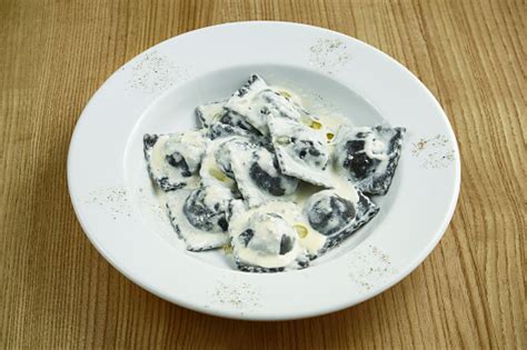 버섯이나 고기로 채워진 식욕을 돋우고 수제 블랙 라비올리 또는 연어와 리코타 치즈를 나무 배경의 흰색 접시에 얹어 먹습니다 이탈리아 요리 음식 닫기 0명에 대한 스톡 사진