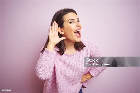 젊은 아름 다운 갈색 머리 여자 분홍색 고립 된 배경 위에 스웨터를 입고 소문 이나 험담에 청각을 듣고 귀에 손으로 미소 청각