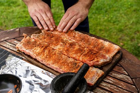 나무 뒤뜰 테이블에 바베큐 돼지 갈비 남자 요리사의 손은 원시 예비 리브에 소금과 향신료를 넣습니다 그릴 흡연 베이킹 및 로스팅을위한 바베큐 준비 과정 라이프 스타일 개념