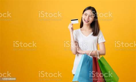 밝은 노란색 배경에 여러 가지 색깔의 쇼핑 백과 신용 카드를 들고 쾌활한 아름다운 아시아 여성 가방에 대한 스톡 사진 및 기타
