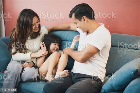 행복 한 쾌활 한 웃는 젊은 가족 어머니 아버지와 딸이 파란색 소파에 앉아서 모두 함께 연주 로즈 핑크 컬러 배경 벽 집에서