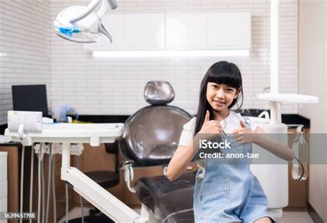건강한 치아를 위한 어린이 치과 클로즈업 행복한 어린 아시아 소녀는 카메라를 보며 미소를 짓고 치과 의사의 의자에 앉아 치과를