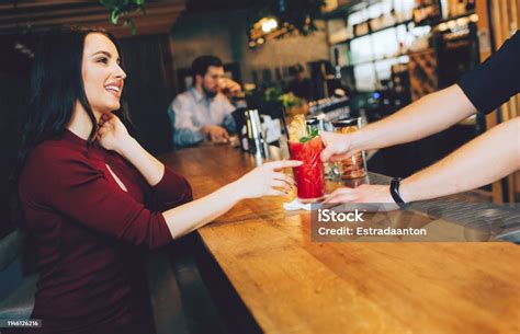 매력적이 고 화려한 여자 스탠드에 앉아서 Barman에서 그녀의 순서를 점점 레드 칵테일입니다 그녀는 바라만을 바라보 며 웃 고