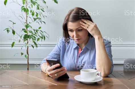 집에서 테이블에 앉아 스마트 폰을 가진 심각한 중년 여성 성년 여자에 대한 스톡 사진 및 기타 이미지 성년 여자 전화 사용