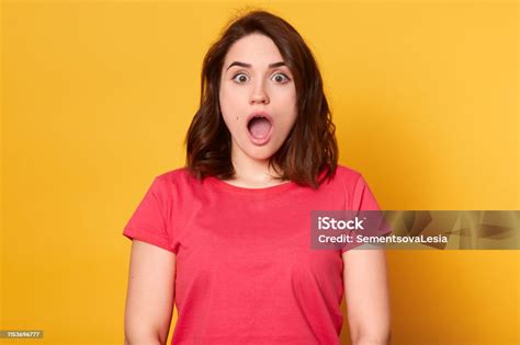 깜짝 보고 젊은 갈색 머리 여자의 초상화를 닫습니다 넓은 열린 입으로 서 노란색 배경 위에 고립 된 빨간 T 셔츠를 입고 인간의