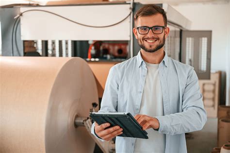 시트 절단기 근처에 서 있을 때 디지털 태블릿을 들고 있습니다 흰 옷을 입은 인쇄소 직원이 실내에 있다 20 24세에 대한 스톡 사진 및 기타 이미지 Istock