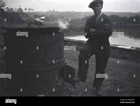 1950s Historical A Man In Work Overalls And Flat Cap Standing Ouside