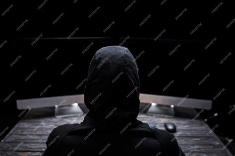 premium photo back view of hooded hacker sitting near computer