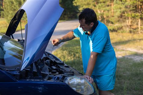 잘 생긴 남자가 도로에서 고장난 자동차의 열린 후드 앞에 서서 수리하려고합니다 가족 여행 중에 차가 고장 나서 남자는 그것을 고치려고합니다 검사 보기에 대한 스톡 사진 및