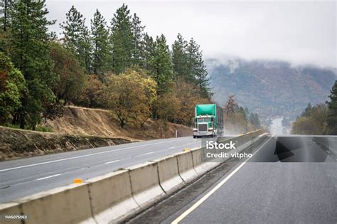 그린 클래식 아메리칸 아이돌 빅 리그 세미 트릭 젖은 안개가 자욱한 고속도로 도로에서 오르막길을 오르는 프론트 스포일러가 있는 덮인 세미 트레일러에서 화물을 운송합니다 세미