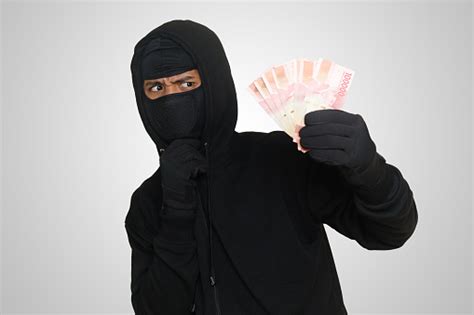 검은 후드티를 입고 가면을 쓴 수수께끼의 남자가 희생자에게서 십만 루피아를 성공적으로 훔치는 초상화 회색 배경에 격리된 이미지