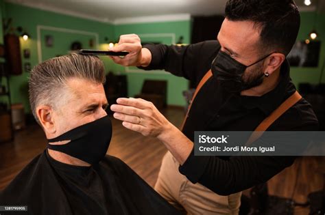 이발사는 손과 빗으로 성인 남성을 빗질하고 마스크 전염병 예방 코로나바이러스를 착용합니다 2명에 대한 스톡 사진 및 기타 이미지
