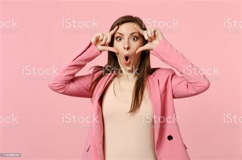 충격 젊은 여자의 초상화는 입을 열어 유지 하는 재킷을 입고 눈 꺼 풀은 스튜디오에서 파스텔 핑크 벽 배경에 고립 스트레칭