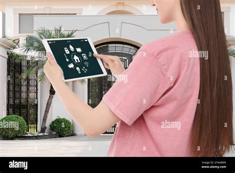Woman Using Smart Home Control System Via Tablet Near House Outdoors
