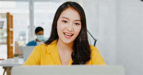 아시아 사업가 사회적 거리두기는 바이러스 예방을 위한 새로운 정상 상황에서 사무실에서 일하는 동안 화상 통화로 계획에 대해 동료들에게 노트북 프레젠테이션을 사용하는 동안