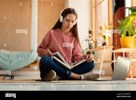 Full Length Portrait Of Focused Teen Girl With Book And Laptop Having Lesson Attending Online