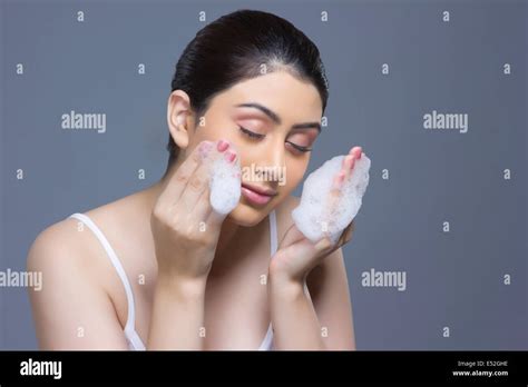 Beautiful Woman Washing Face With Soap Sud Against Blue Background