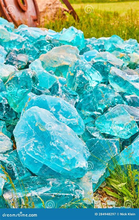 Pile Of Cloudy Blue Glass Crystals Laying In Grassy Field Vertical